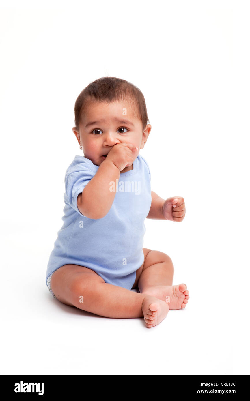Indian baby dressed in blue sitting up sucking thumb Stock Photo - Alamy