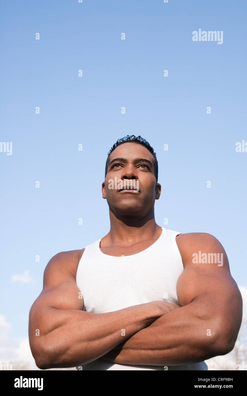 Confident African American bodybuilder with arms crossed against blue ...