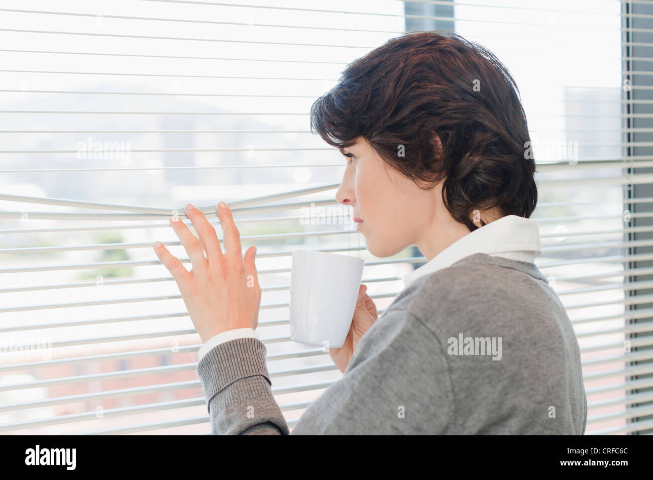 Businesswoman peering out office window Stock Photo - Alamy