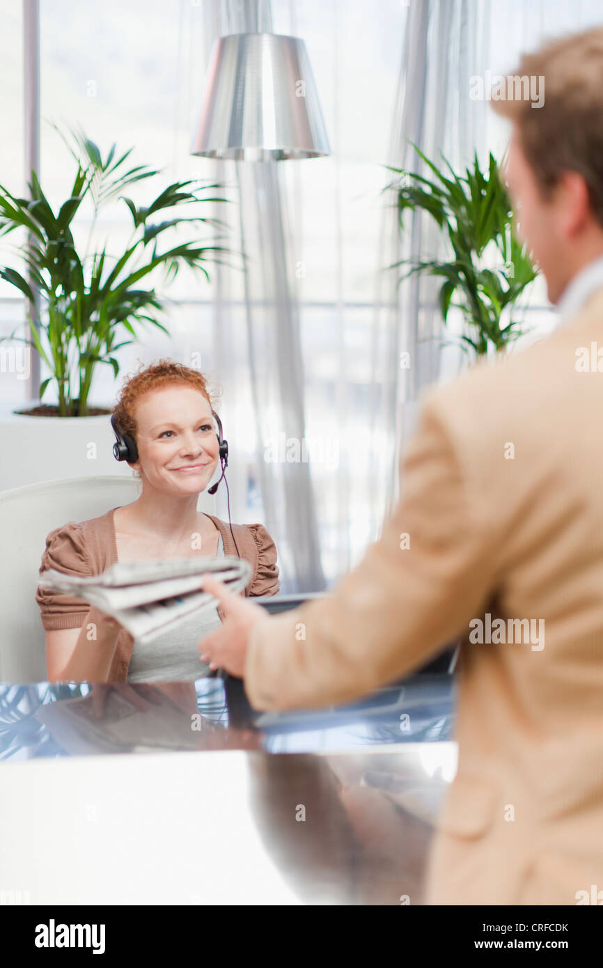 Receptionist giving newspaper to man Stock Photo - Alamy