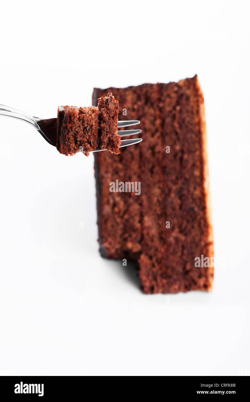 piece of a chocolate cake on a fork over a chocolate cake on white ...