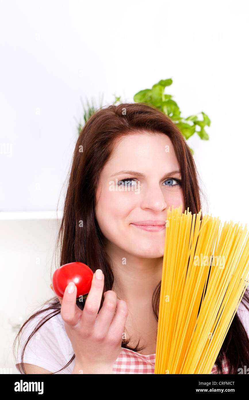 smiling young woman in a kitchen holding spaghetti and tomato Stock ...