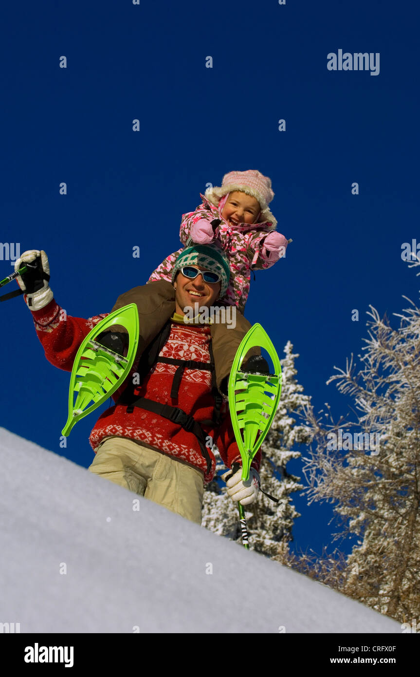 father and daughter with snow shoes. The father carries his daughter ...