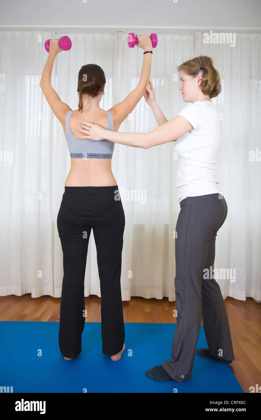 young woman doing exercise with dumb-bells, instructed by a female ...