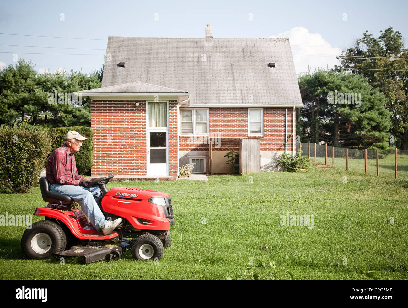 An older man rides a rider lawn mower on a green lawn with a small ...