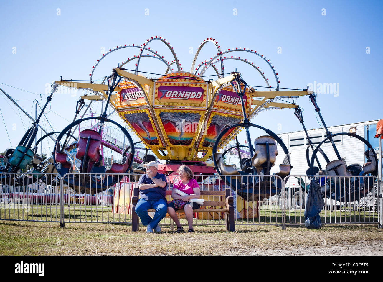 A couple sits on a bench in front of a carnival merry-go-round on a ...