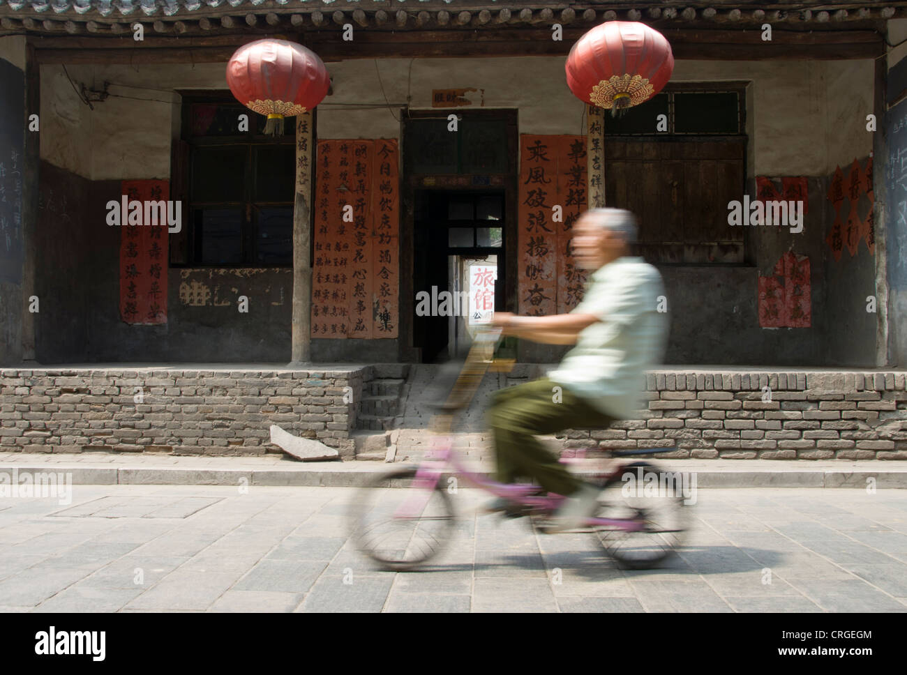 Old Chinese man riding a bike in front of a traditional old street ...