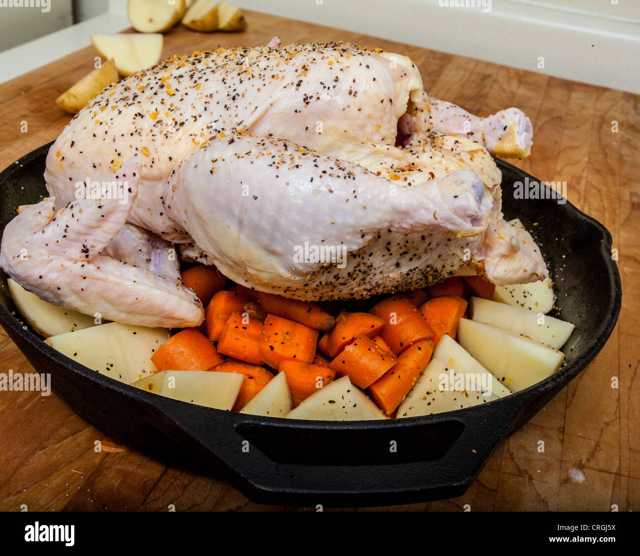 A raw chicken prepared for roasting with potatoes and carrots in a cast ...