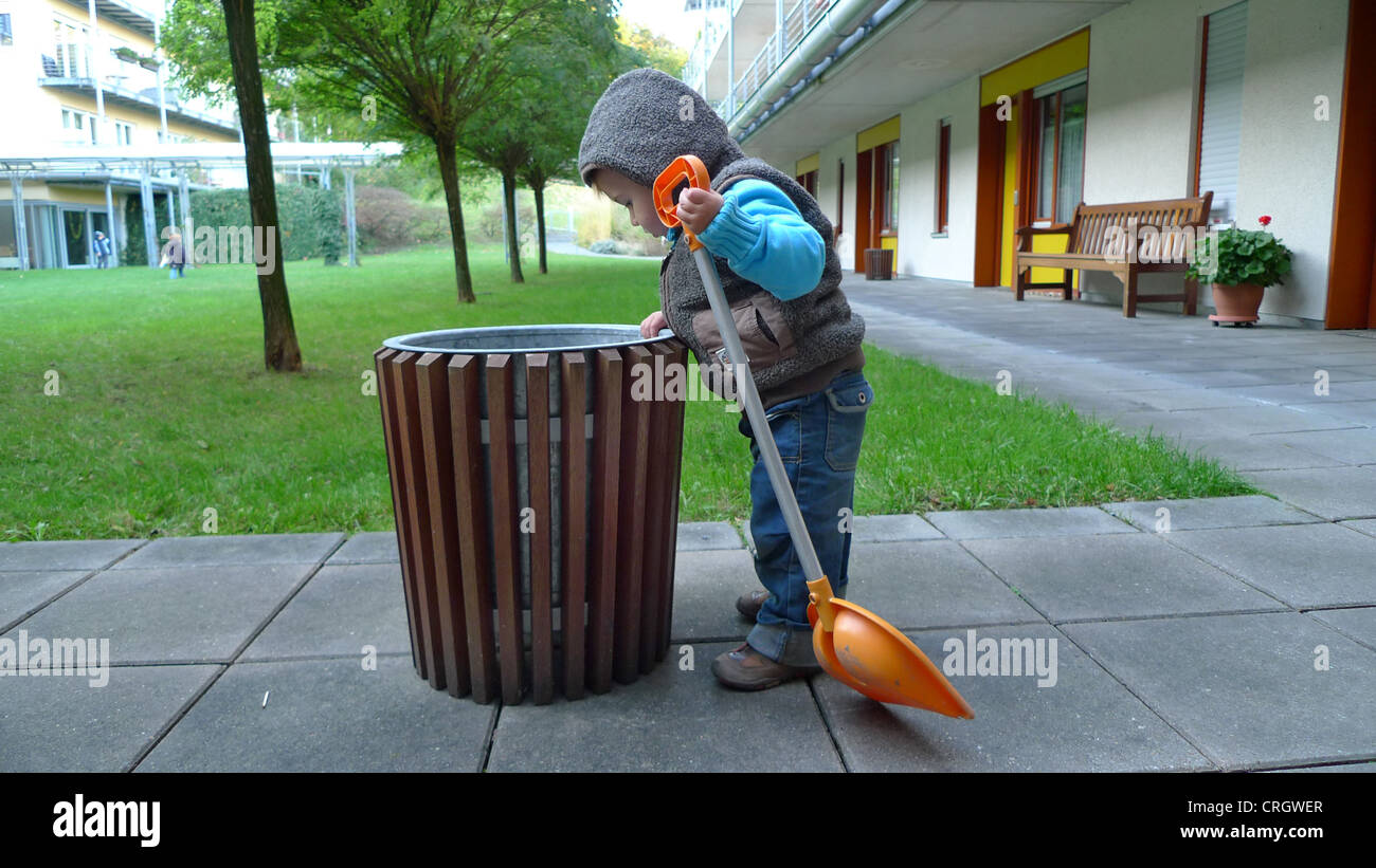 little child with a children's shovel looking into a dustbin Stock ...