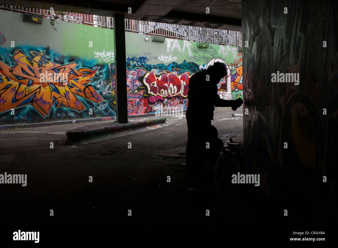 Sinister graffiti artist silhouette sprays walls in underpass tunnel in ...