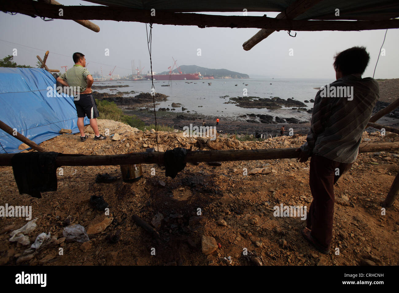 Men watch as thick oil sludge coat the shore during the oil spill ...