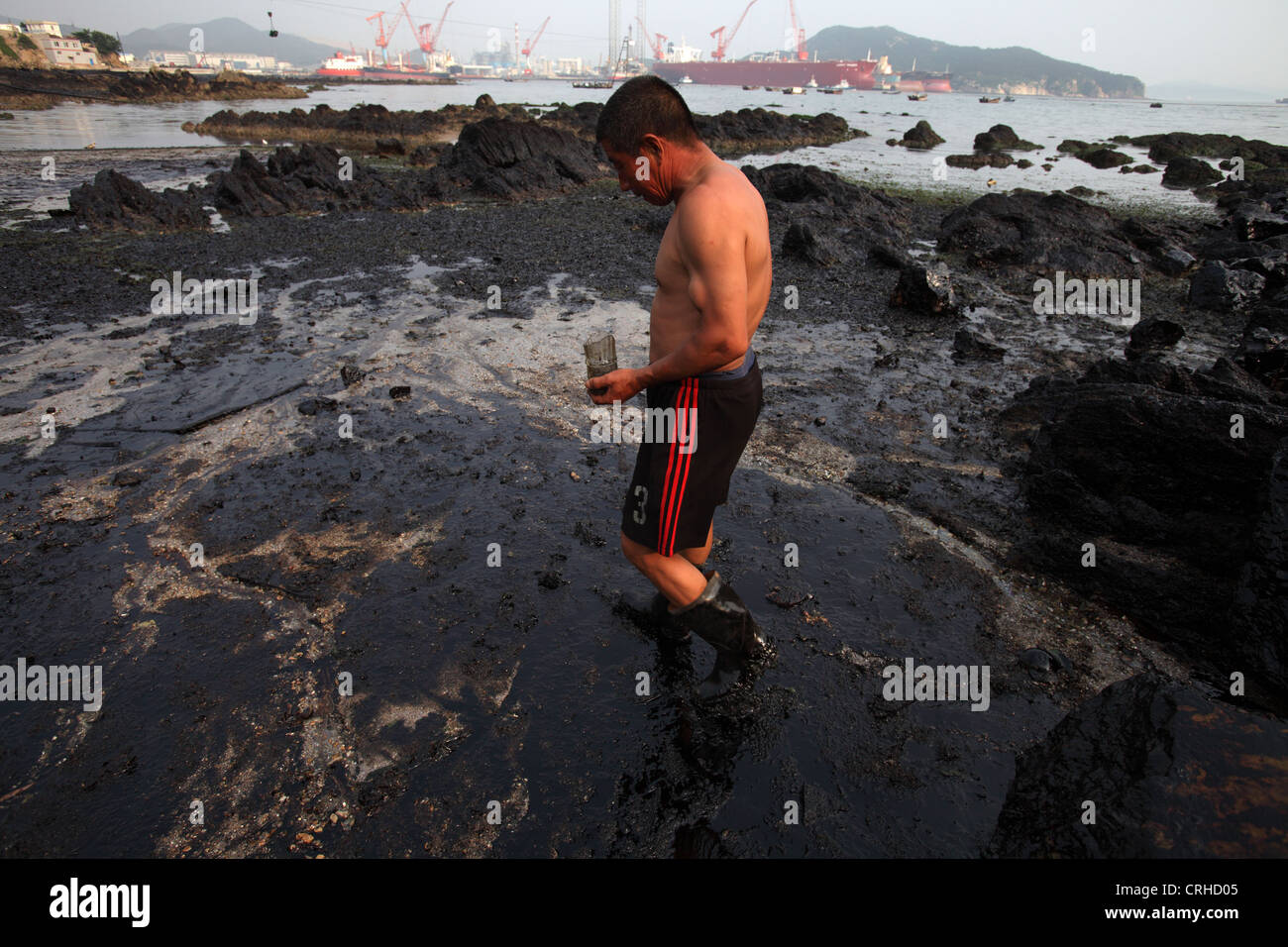 A man walks through oil sludge during the oil spill disaster in Dalian ...