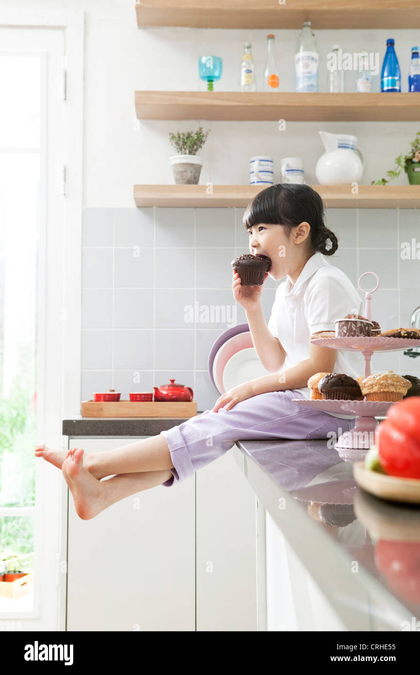 Little girl having muffin sitting on kitchen counter Stock Photo - Alamy