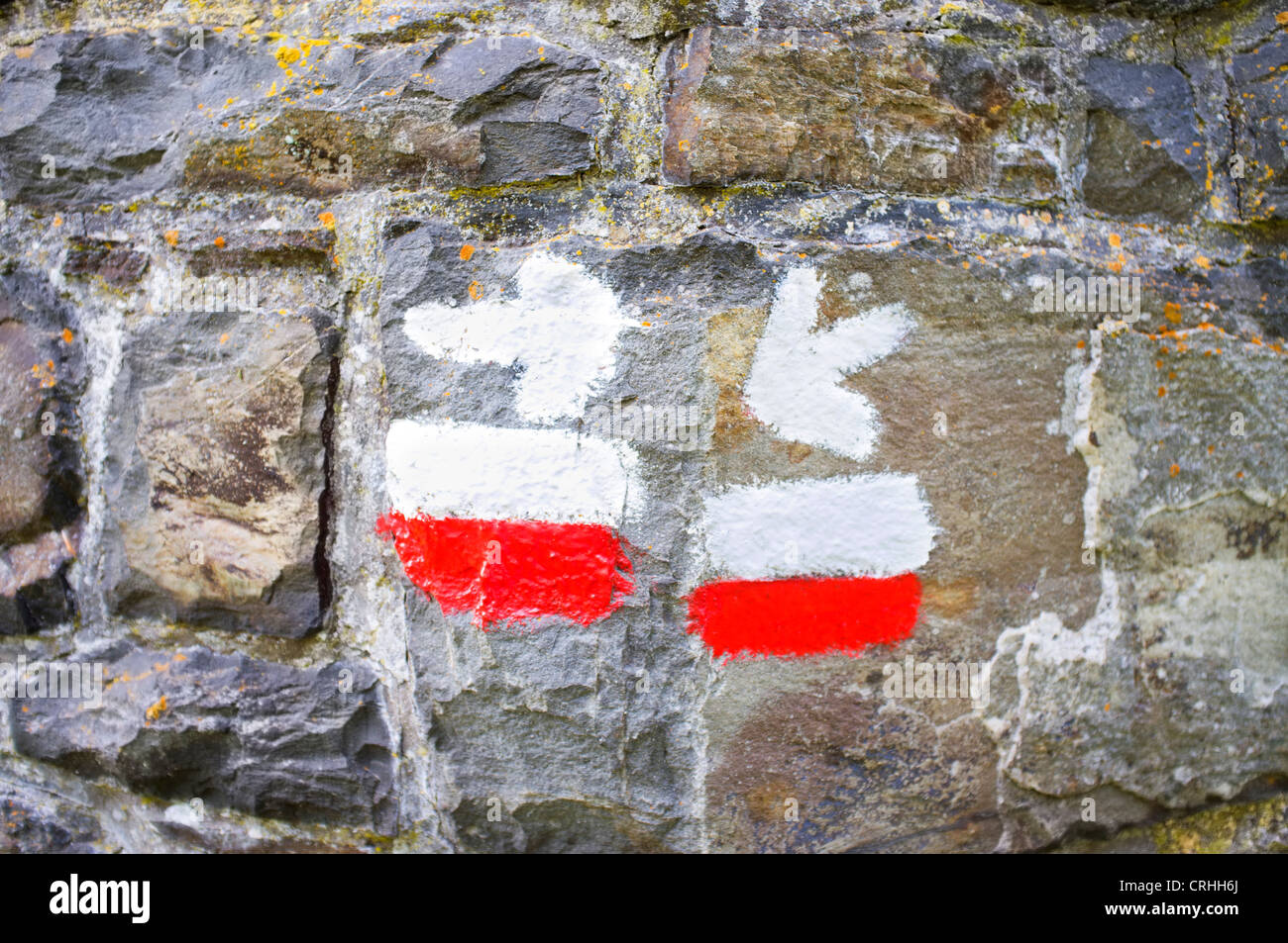 Directional arrow sign on a stone wall, with the white and red stripes ...