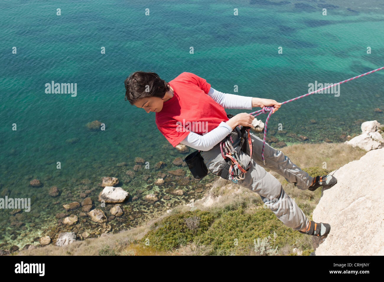 Woman climbing rocky coastal cliff Stock Photo - Alamy