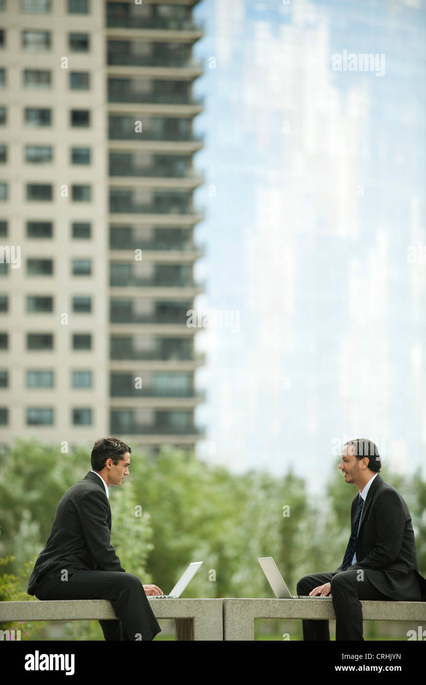 Business executives discussing work while using laptop computers ...