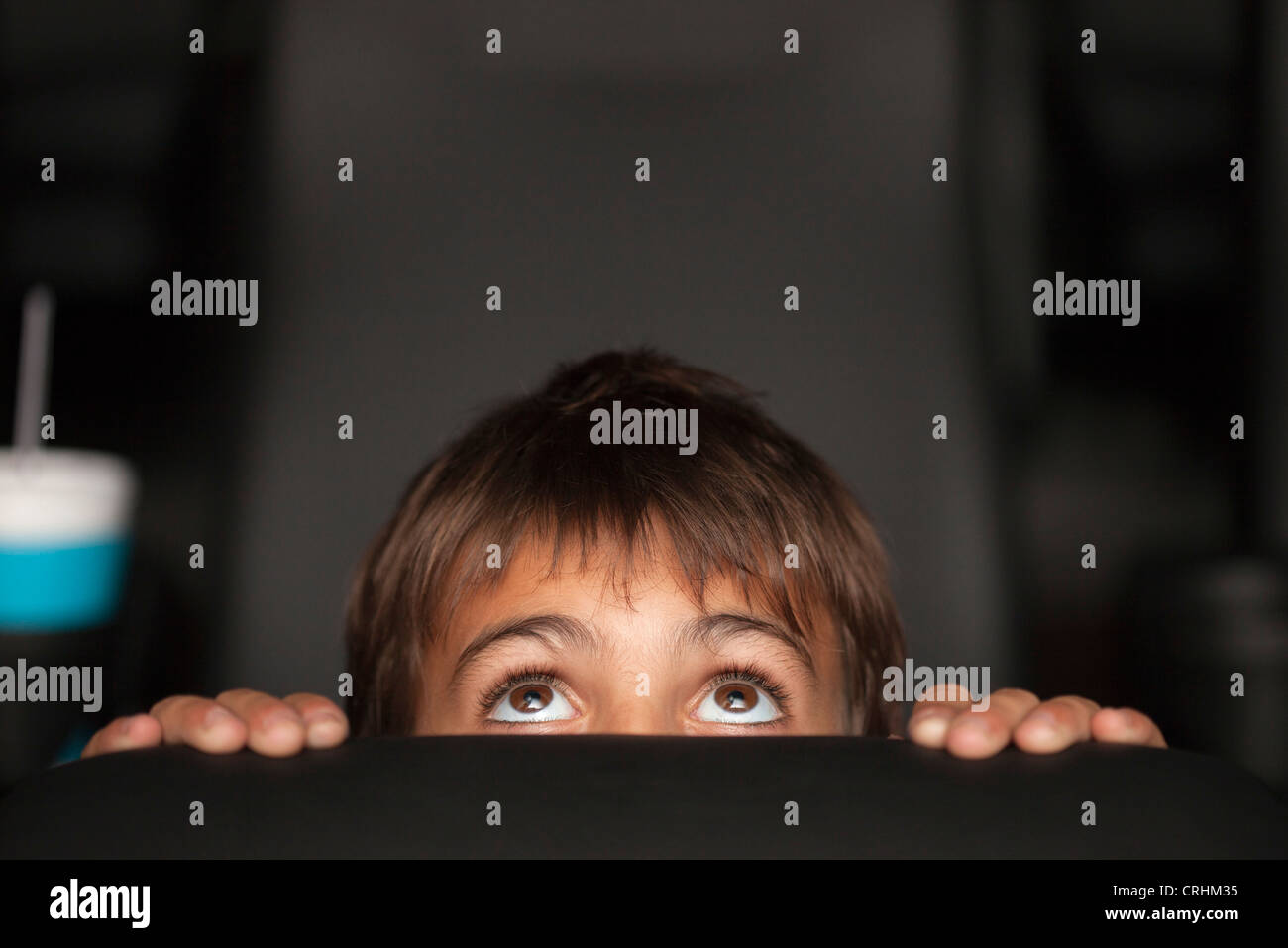 Boy peeking over top of seat during horror movie in theater Stock Photo ...