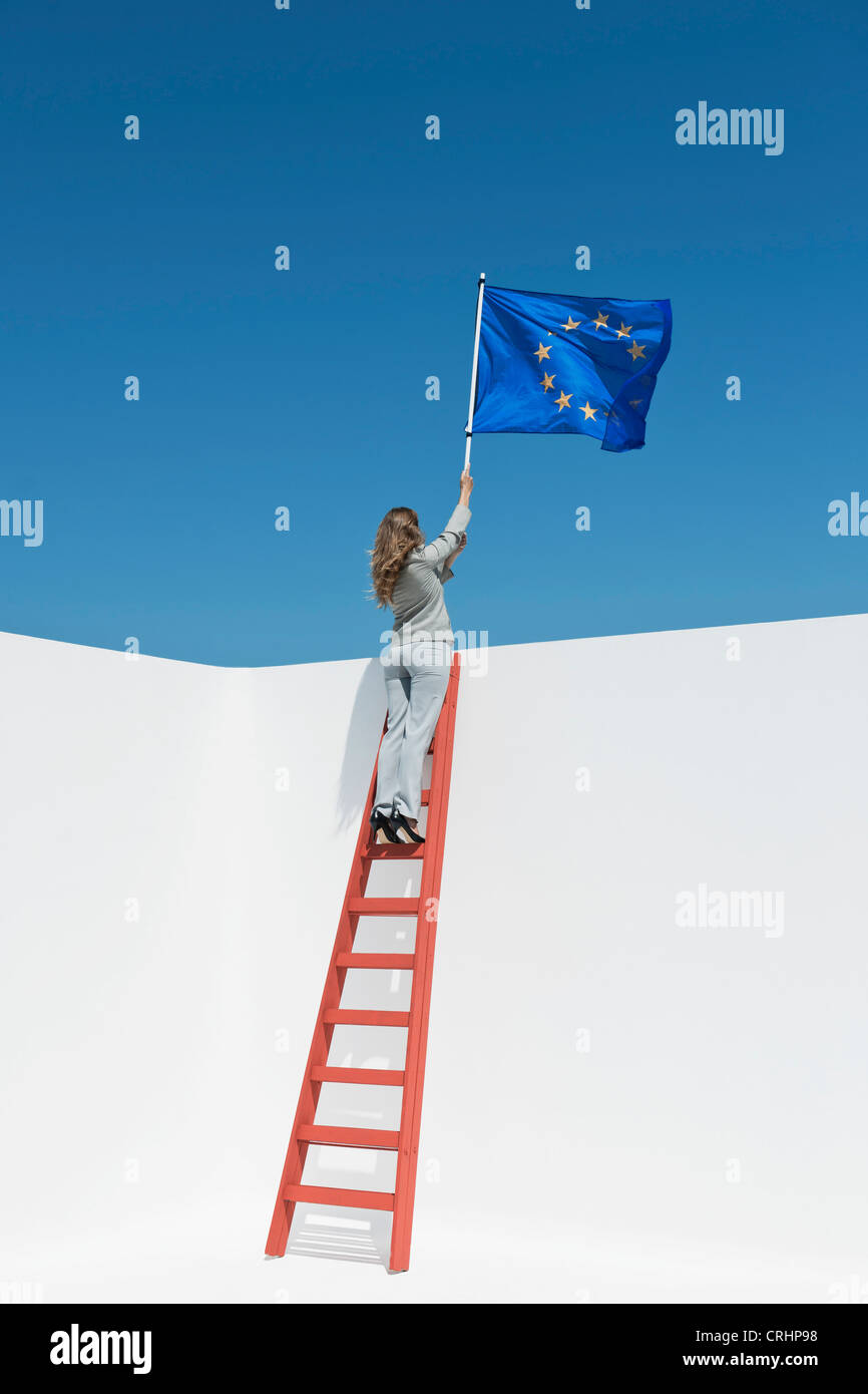 Businesswoman standing at top of ladder, holding European Union flag ...