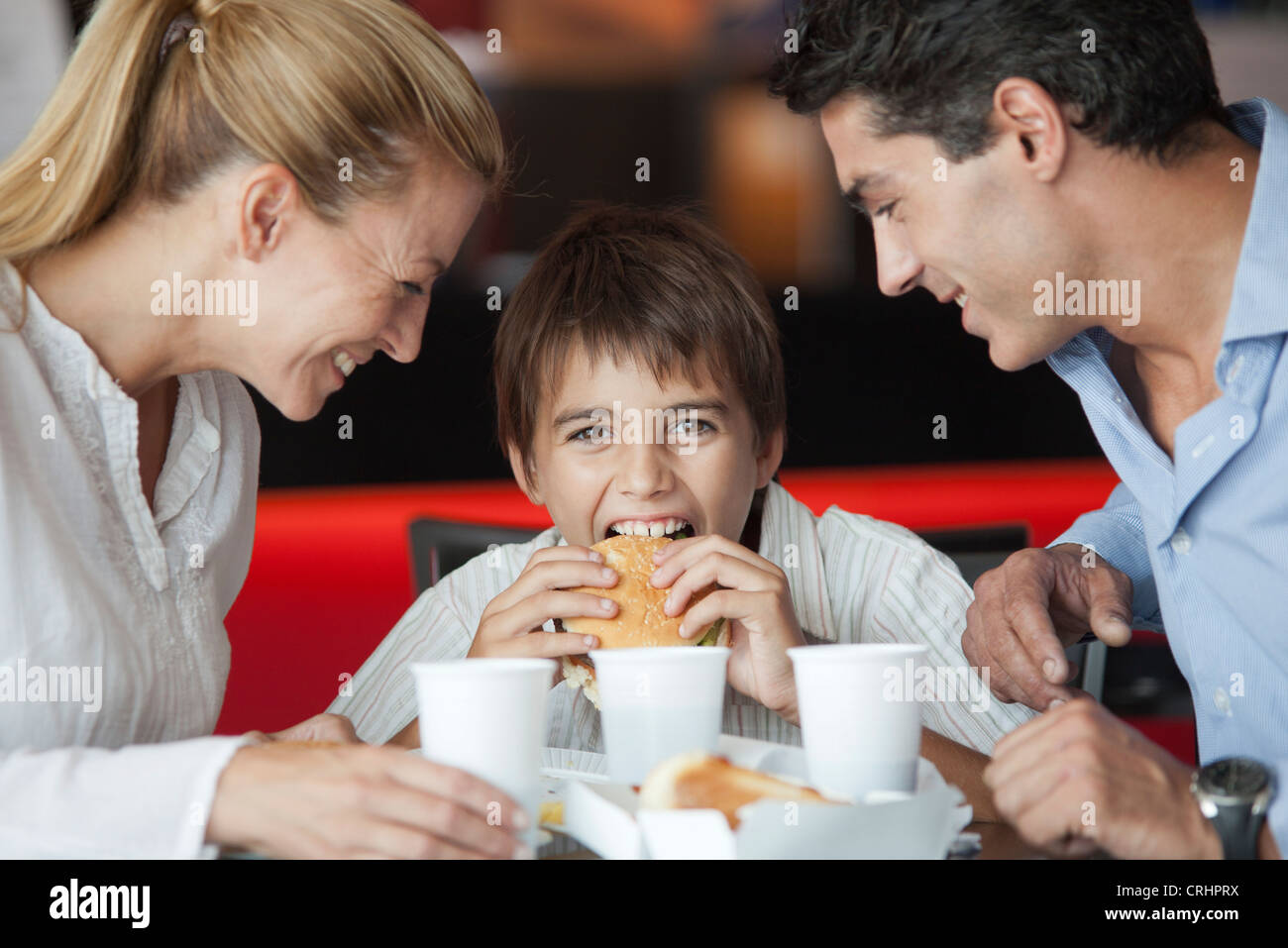 Boy eating hamburger with his parents in fast food restaurant Stock ...