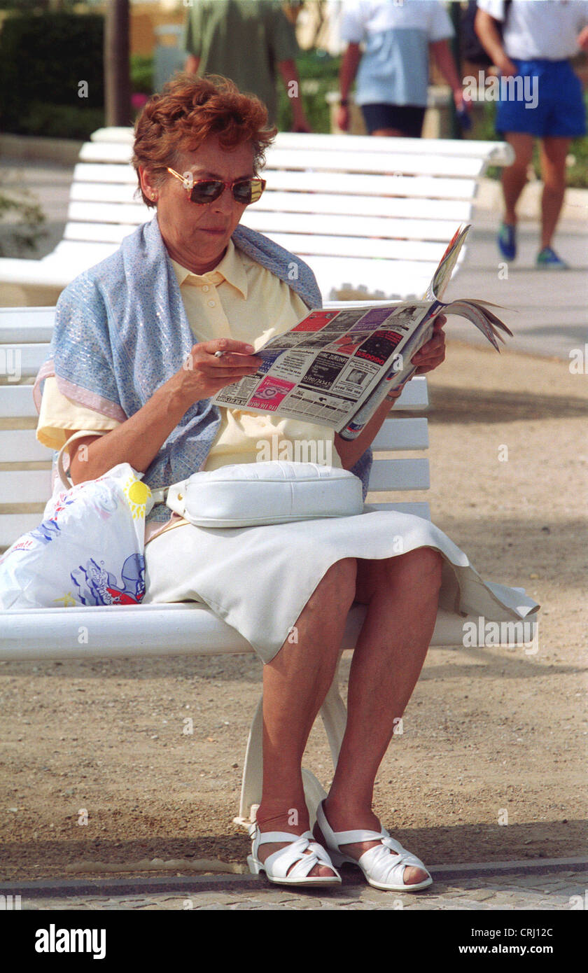 A woman on the beach promenade, reading the newspaper Stock Photo - Alamy