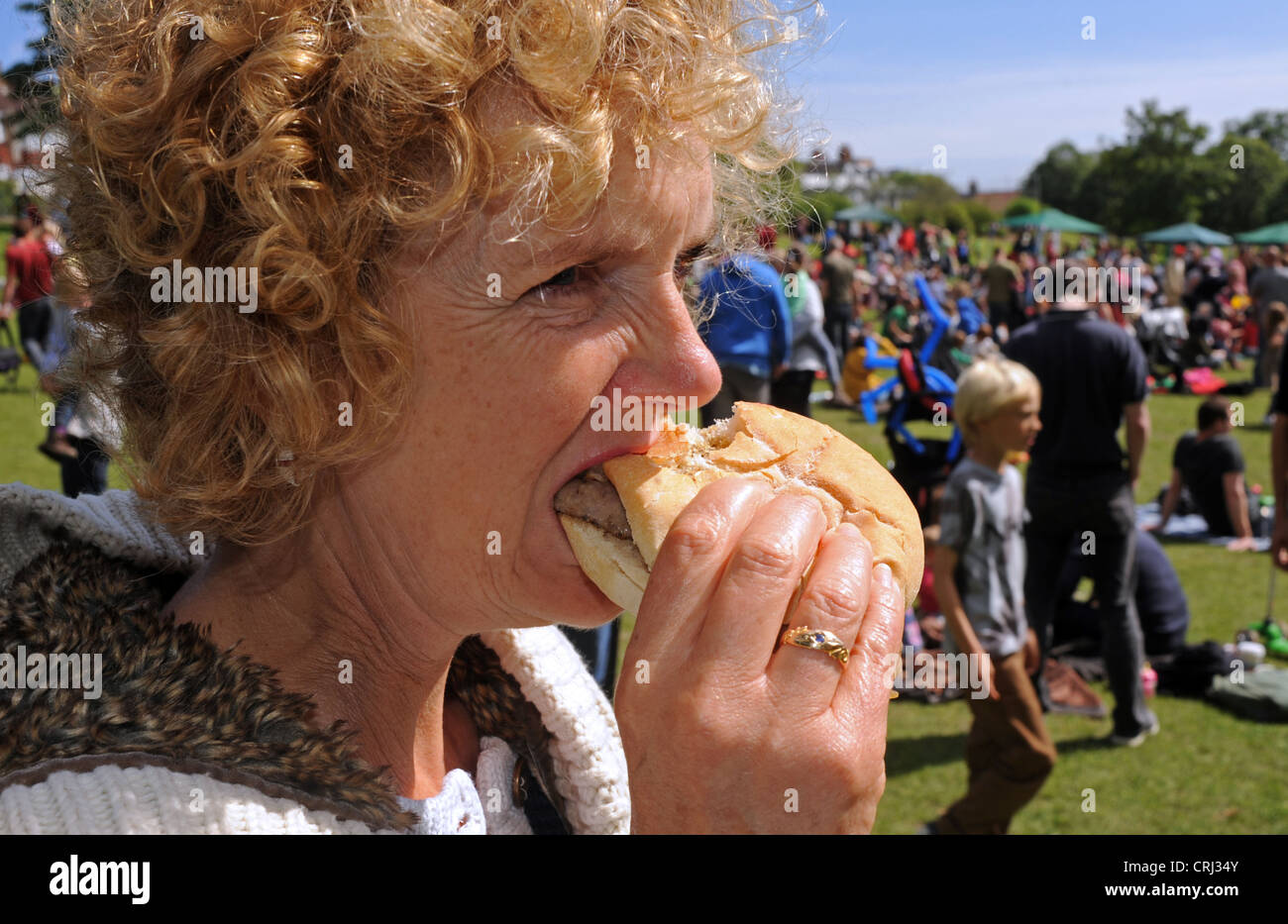 Middle aged woman taking a large bite out of a sausage filled bap roll ...