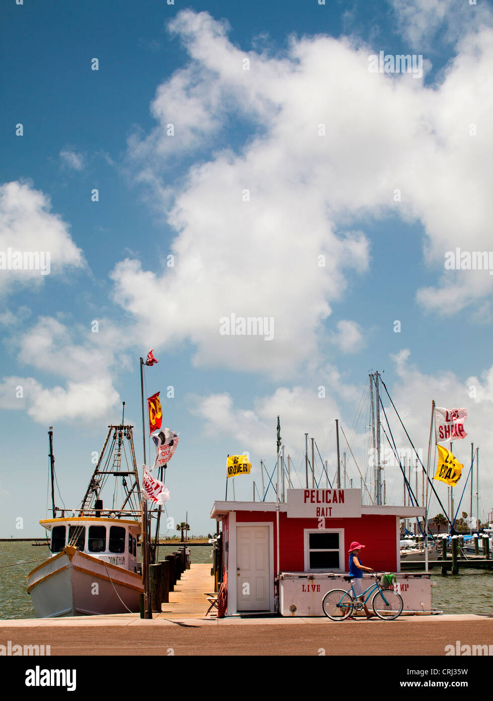 A woman wearing a pink floppy hat walks her bike in front of a fishing ...