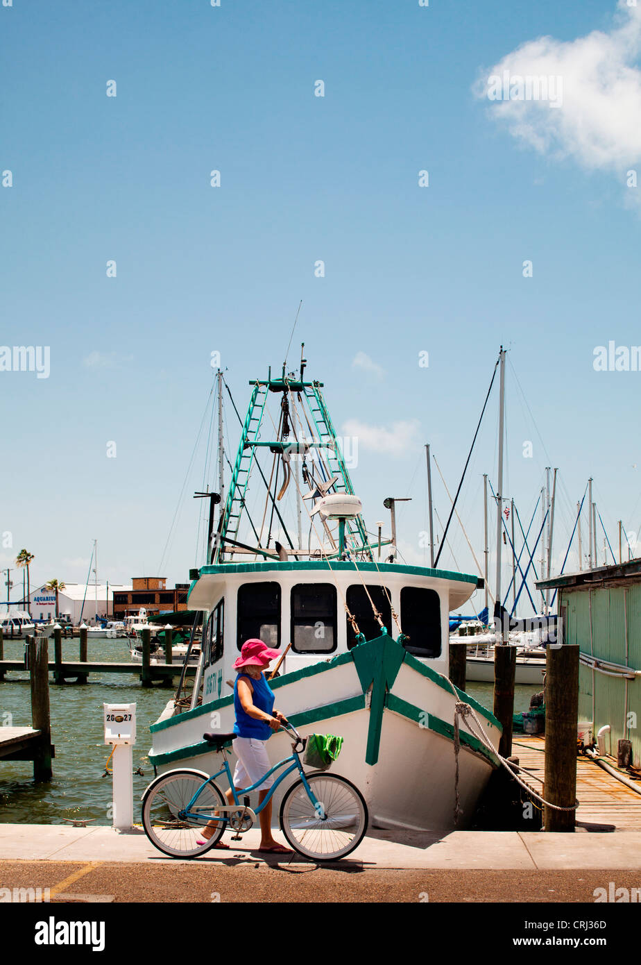 A woman wearing a pink floppy hat walks her bike in front of a fishing ...