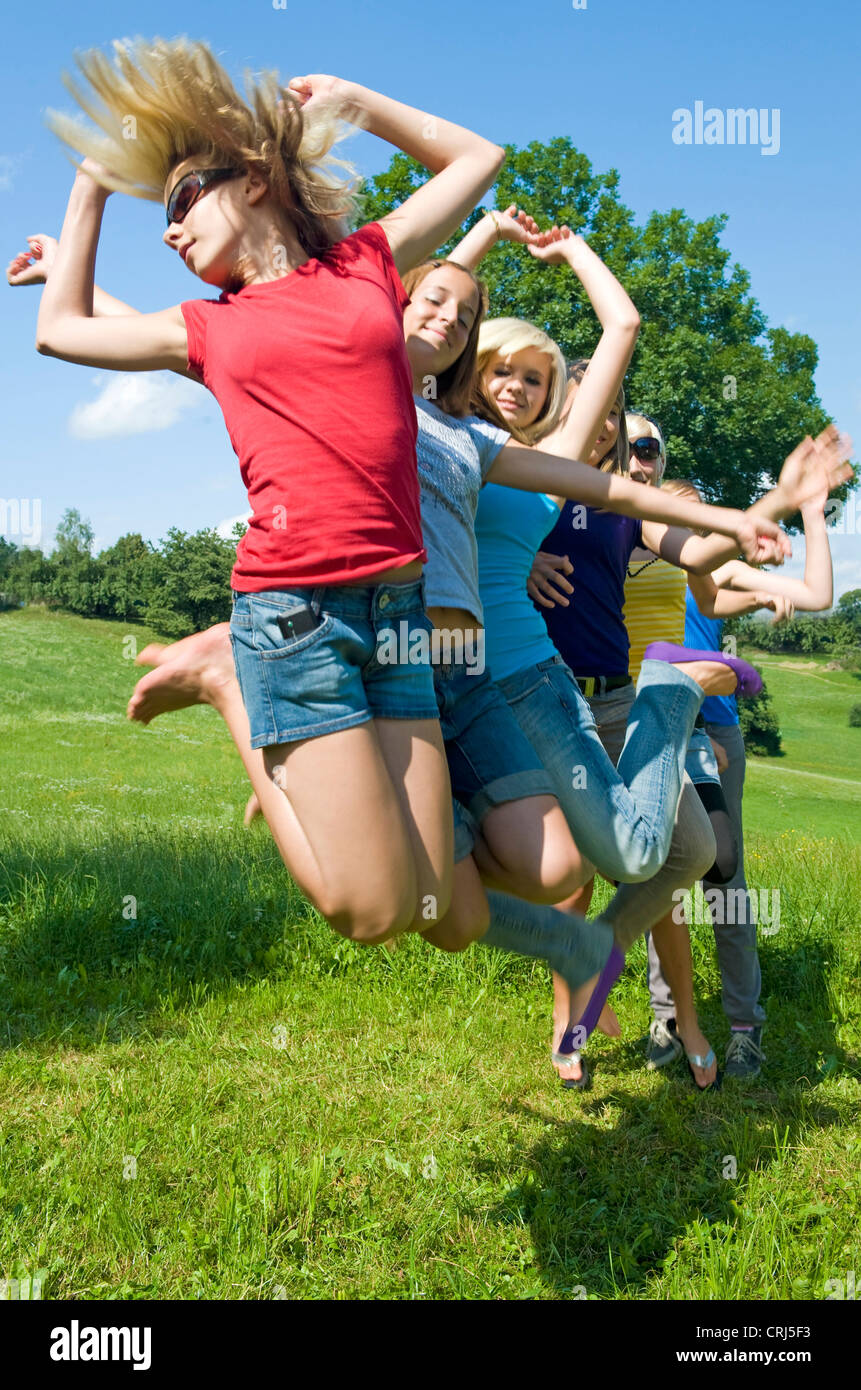 group of teenage girls in a meadow jumping into the air in a row behind ...