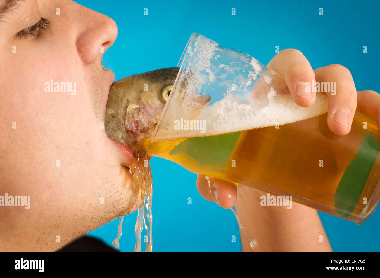 Young man tries to eat a fish and drink a glass of beer at the same ...