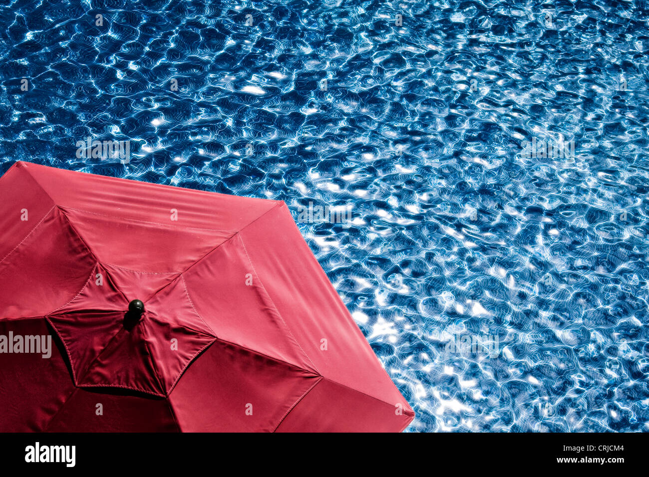 Landscape photograph of a red sun parasol against a pool water ...