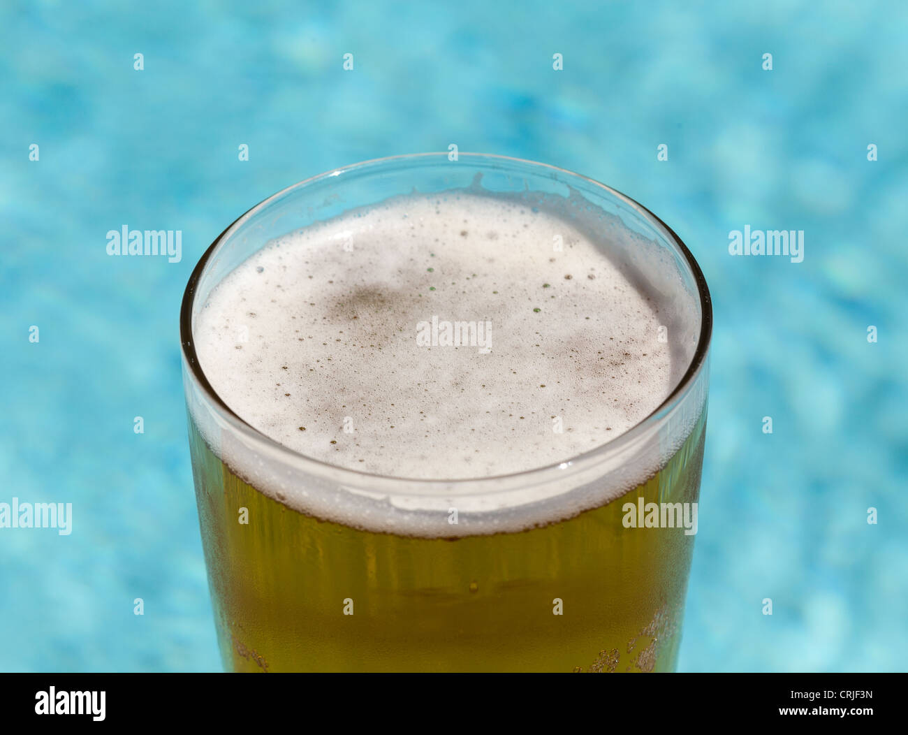 Plain pint glass of cold lager beer sitting on edge of blue swimming ...