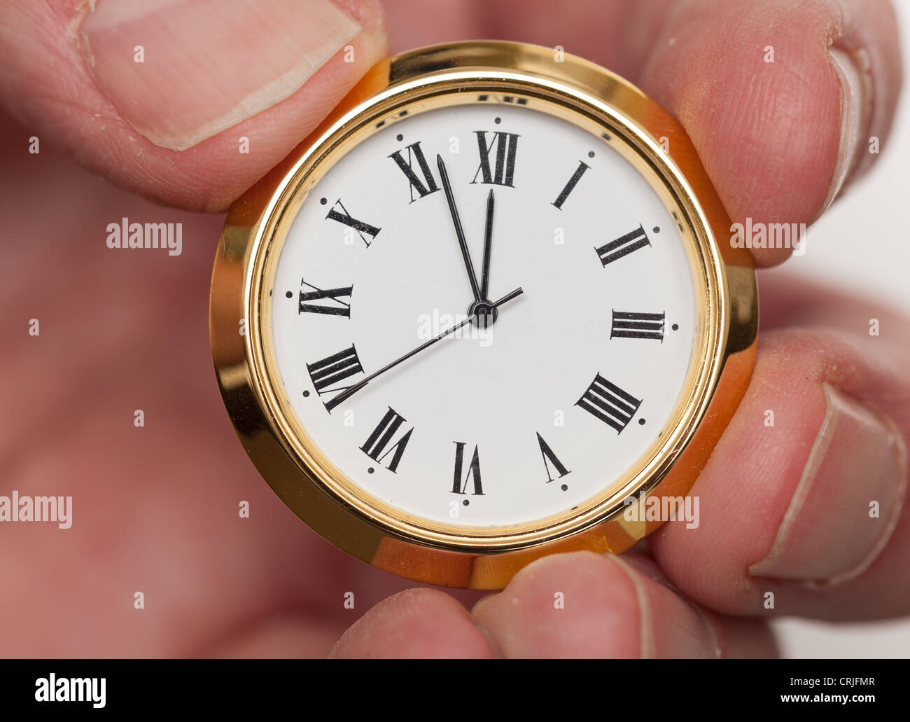 Small gold colored clock almost at midnight held by tips of fingers ...
