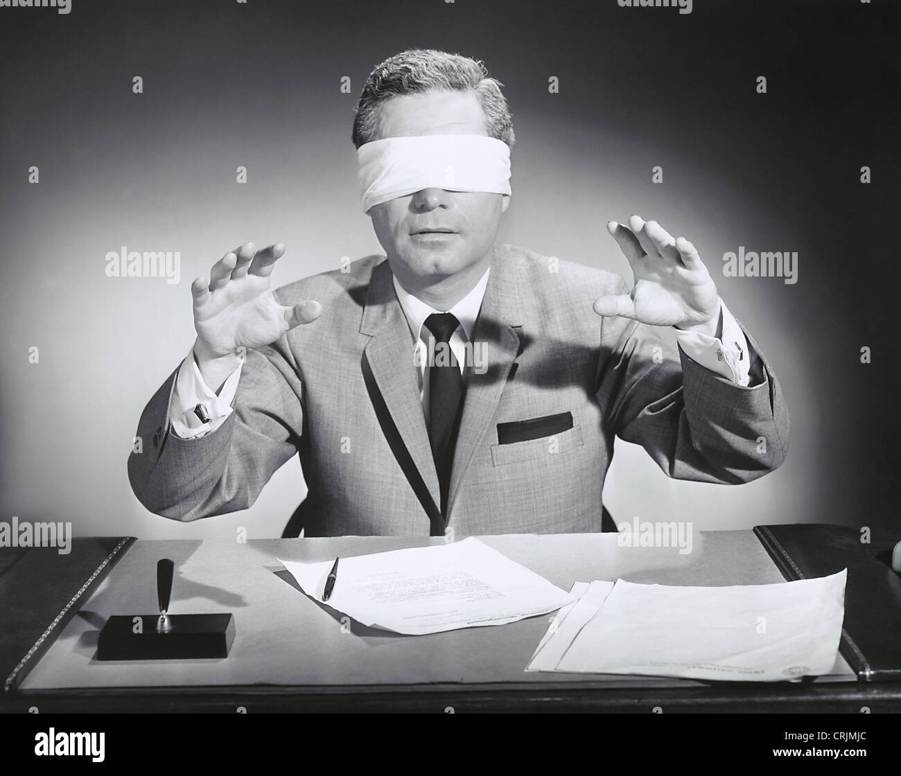 Businessman blindfolded sitting at desk Stock Photo - Alamy
