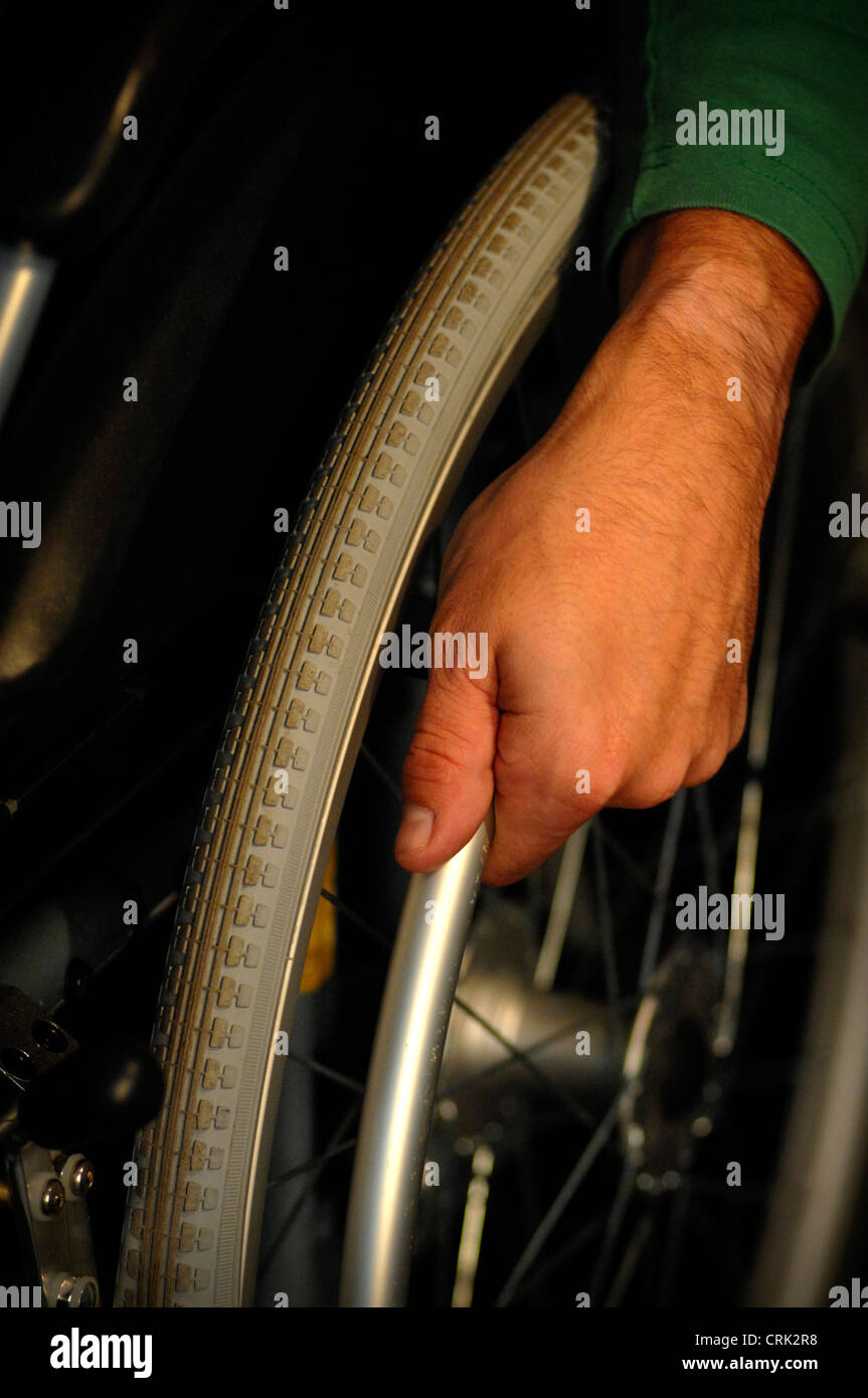 A close-up of the hand of a wheelchair user, using his hand to move his ...
