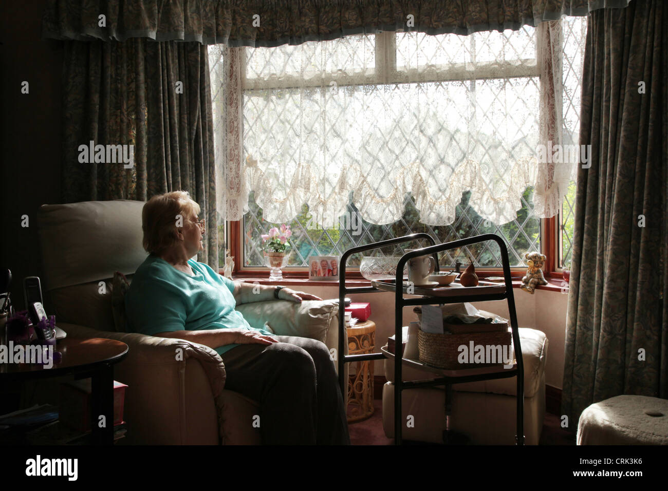Mature woman sitting alone looking out of the window through net ...