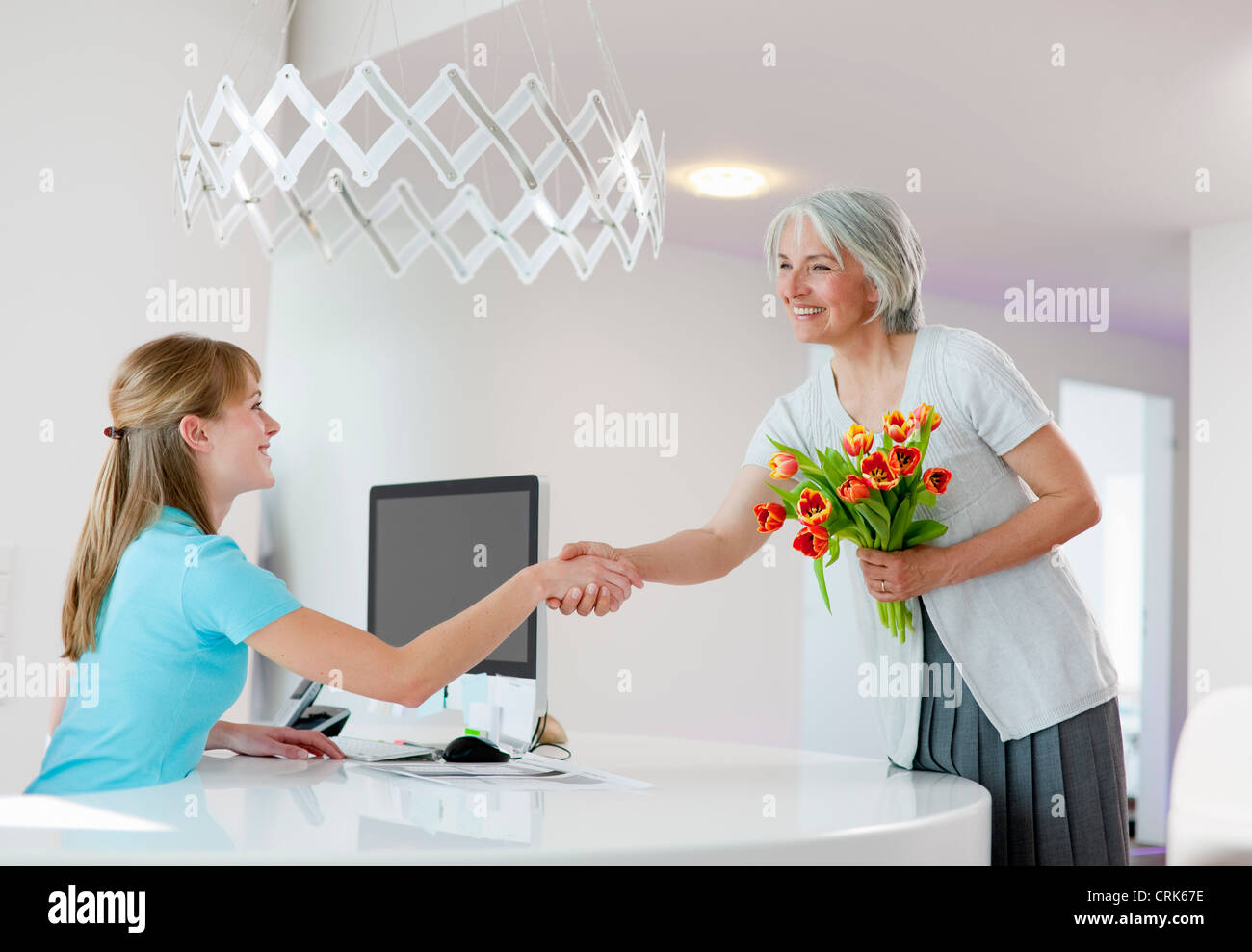 Receptionist shaking womans hand Stock Photo - Alamy