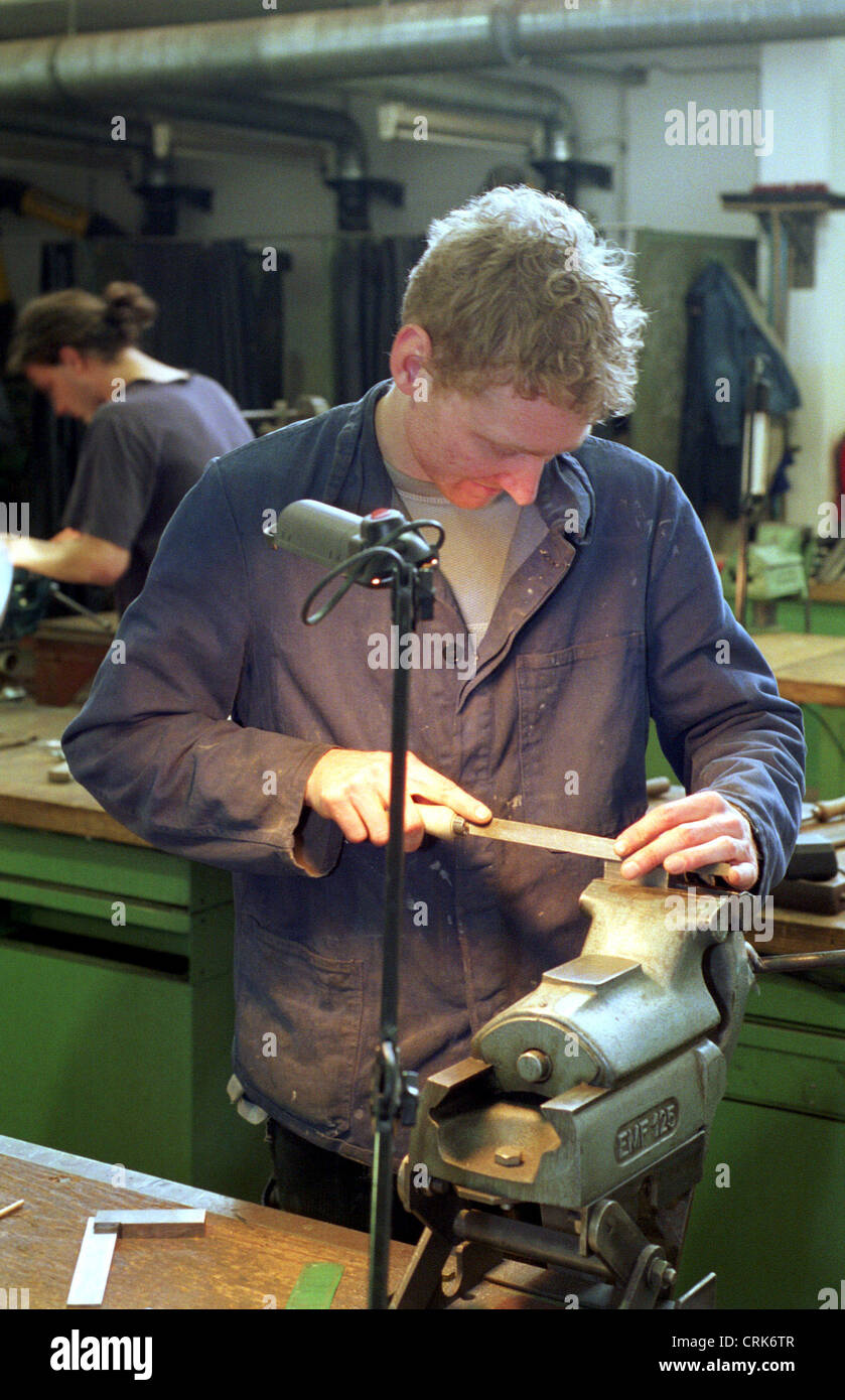 Berlin, an apprentice metal worker stands at a workbench and polishes ...