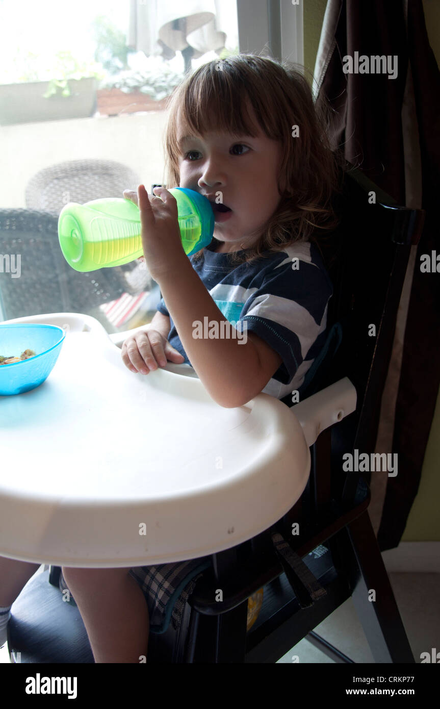 Cute baby boy kid drinking in high chair Stock Photo - Alamy