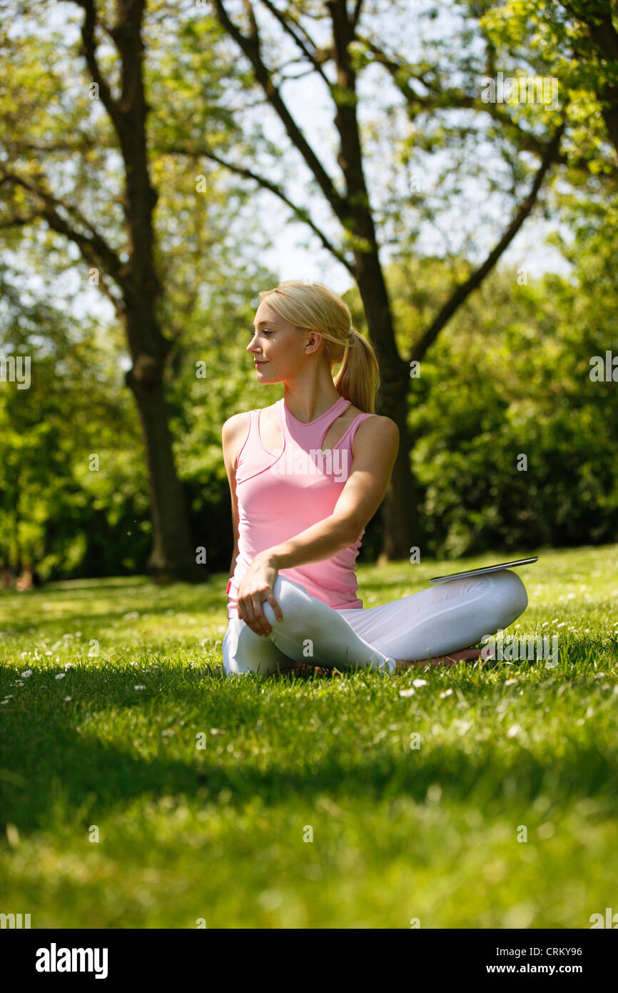 A young blonde woman sitting in the grass, stretching Stock Photo - Alamy