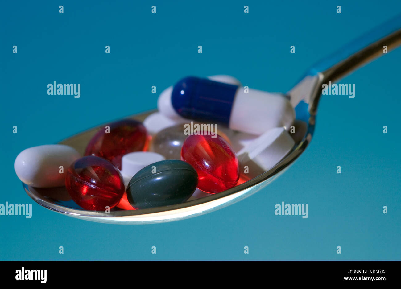 A spoonful of assorted coloured pills and capsules against a blue ...