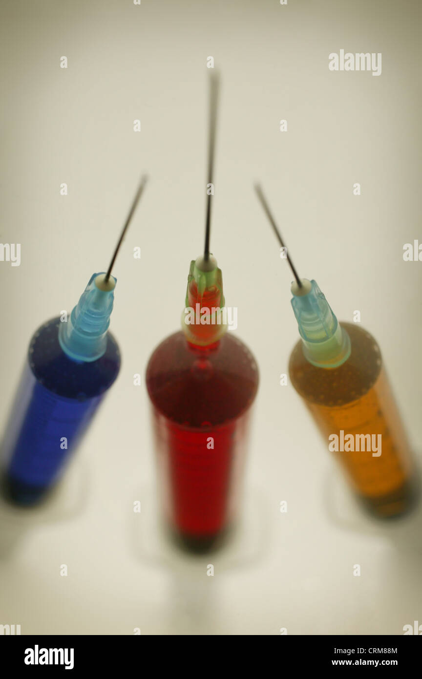 Three disposable hypodermic syringes containing different coloured ...