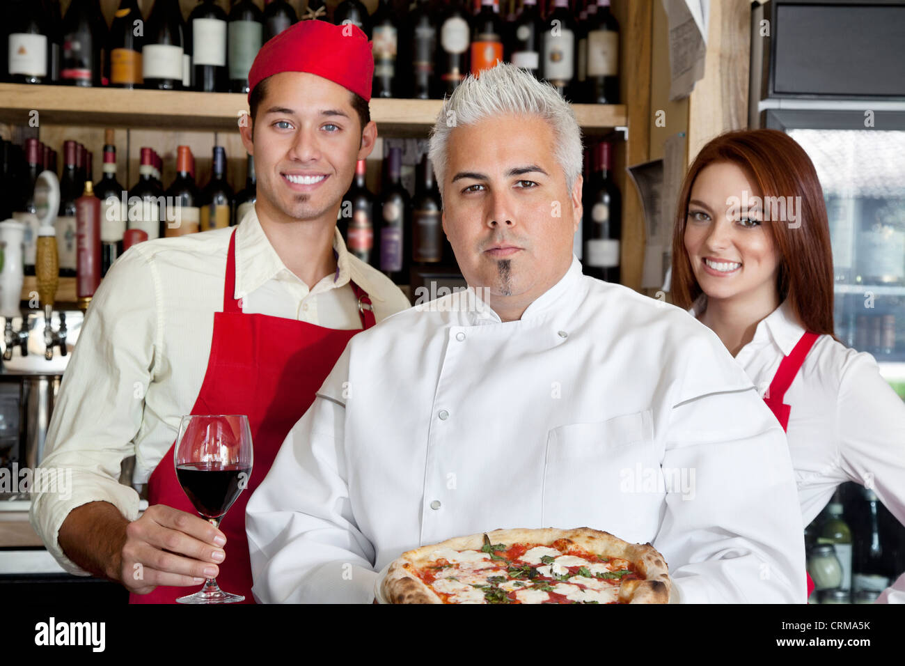 Portrait of a confident chef holding pizza with wait staff in ...