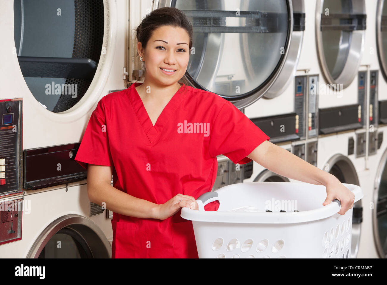 Portrait of a happy woman carrying laundry basket with washing machine ...