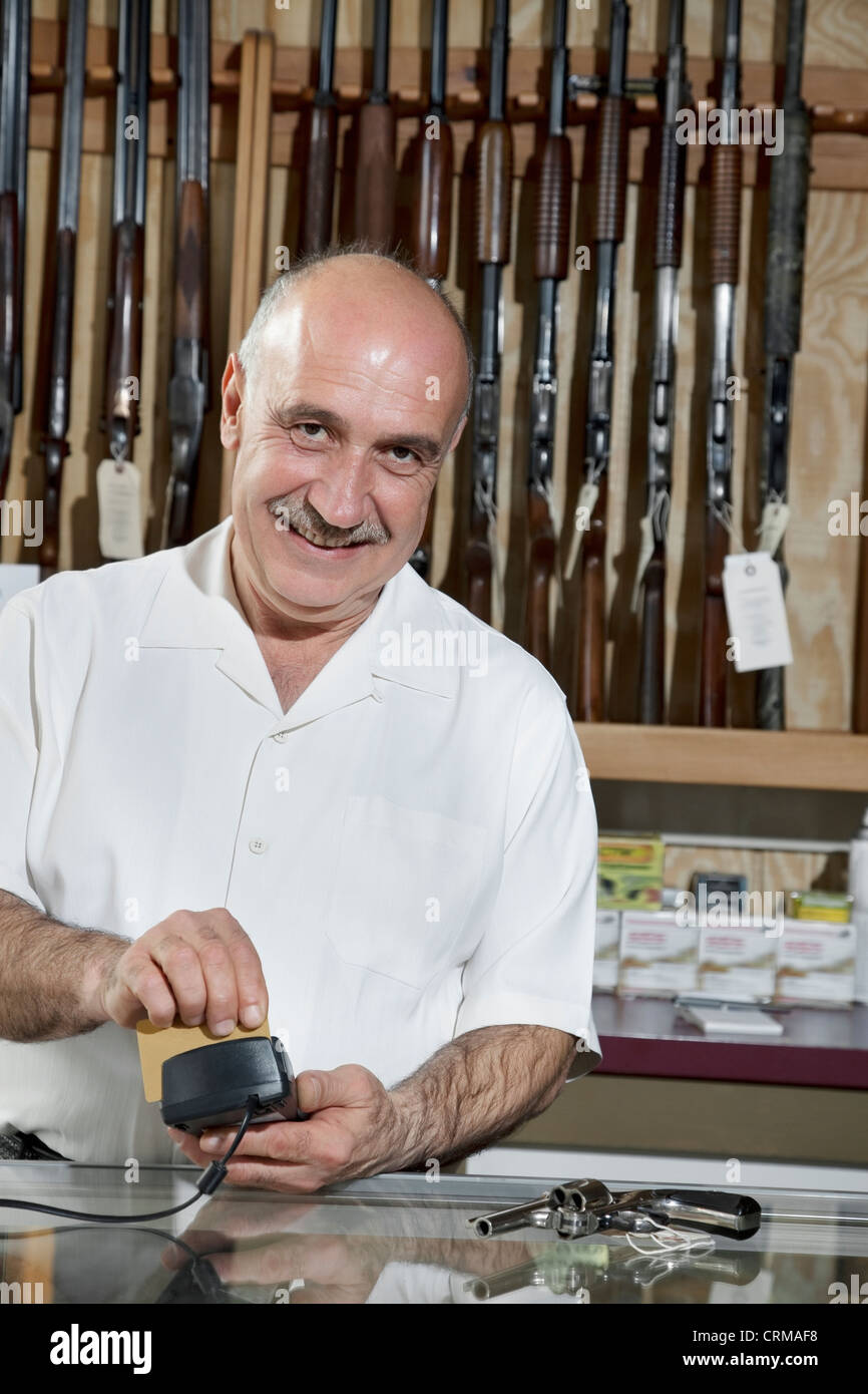 Portrait of a mature merchant with credit card reader in gun shop Stock ...