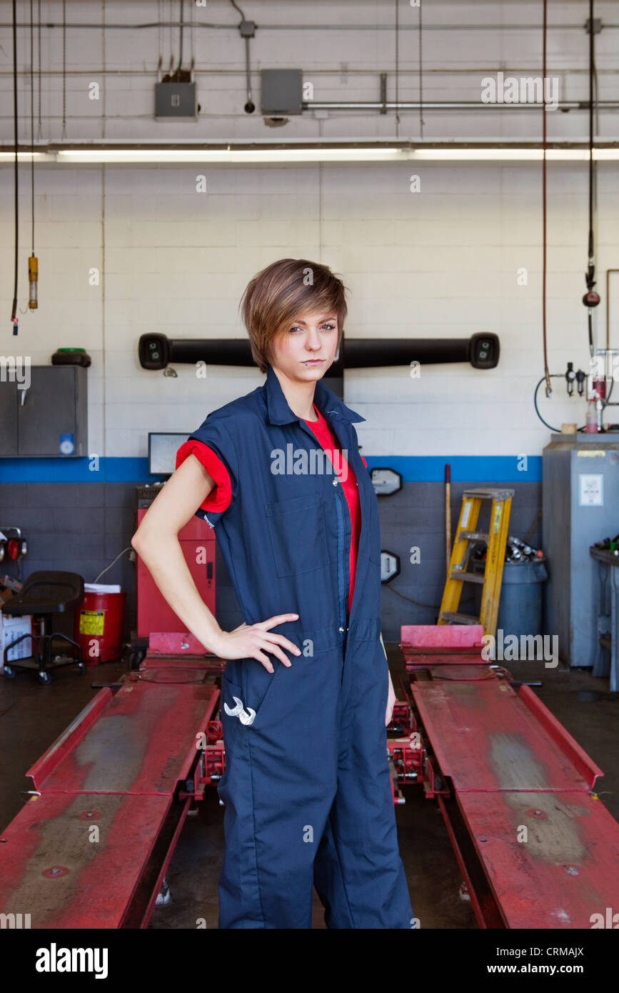 Portrait of a young female mechanic standing with hand on hip in car ...