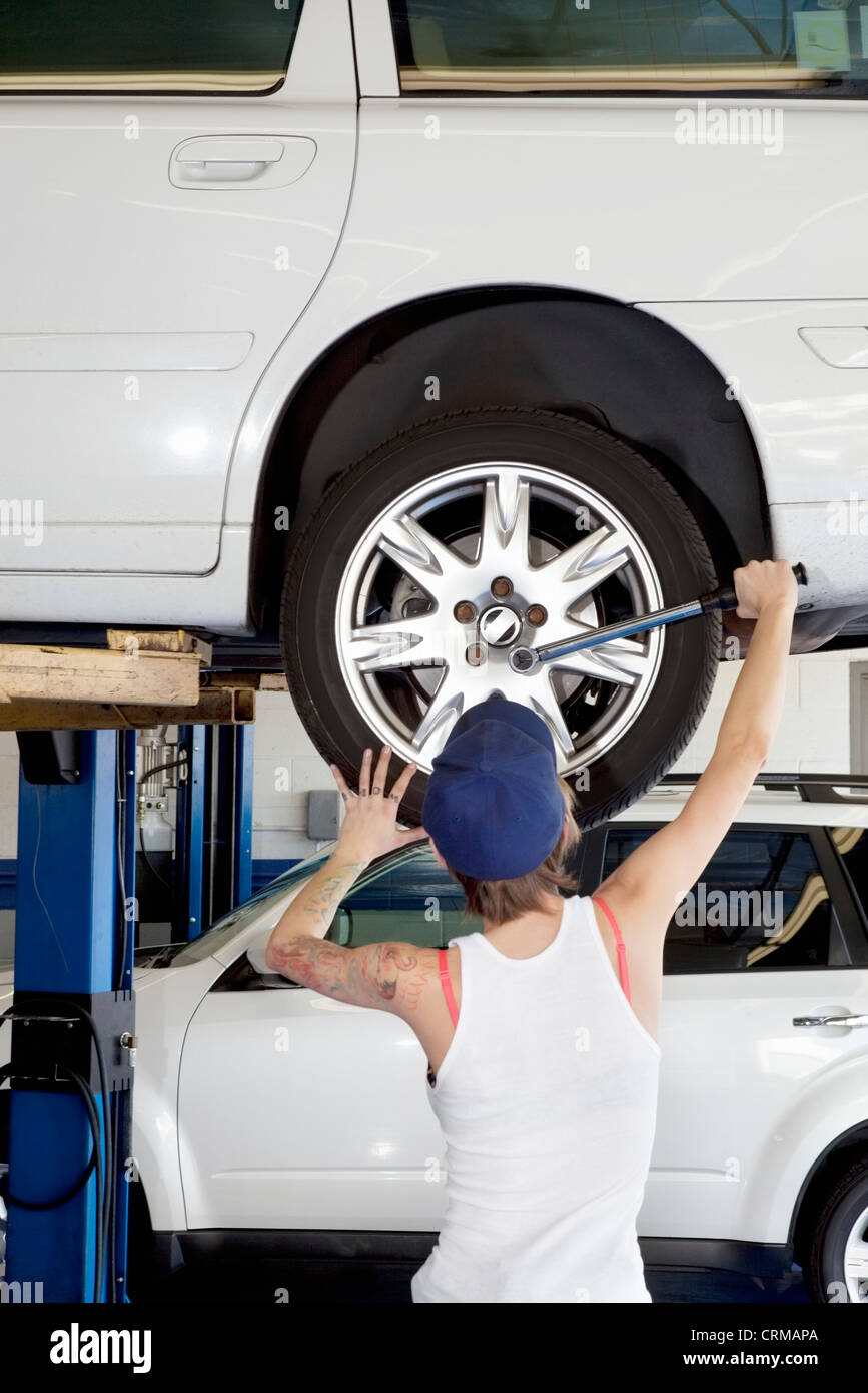 Back view of young female working on car tire in workshop Stock Photo ...