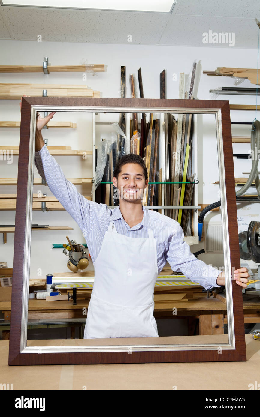 Portrait of a happy young craftsman holding big frame in workshop Stock ...