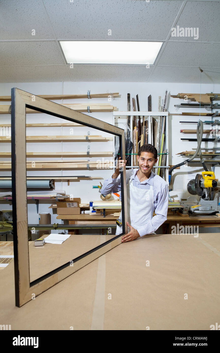 Portrait of a happy young man working on big picture frame in workshop ...