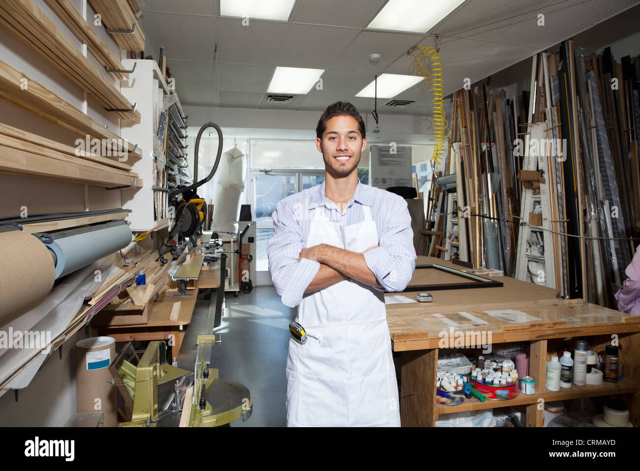 Portrait of a happy young craftsman standing with arms crossed in ...