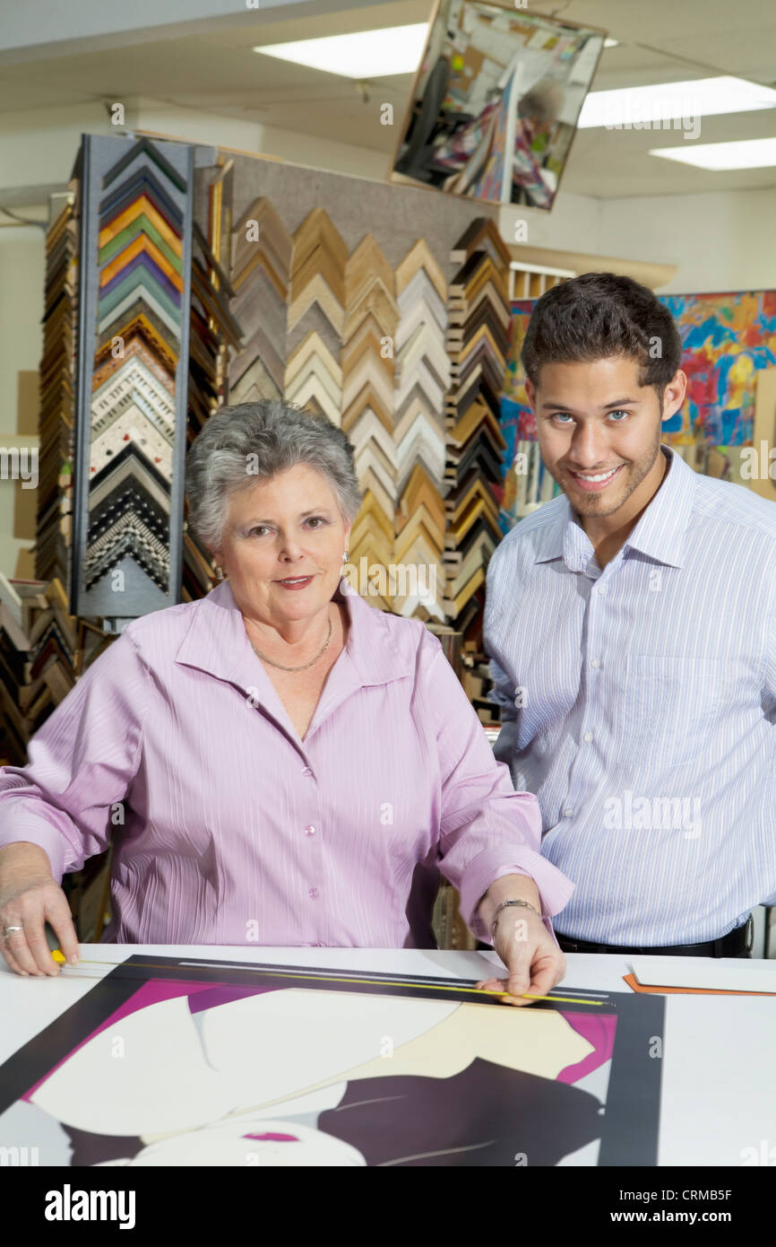 Portrait of senior female owner with customer measuring picture frame ...